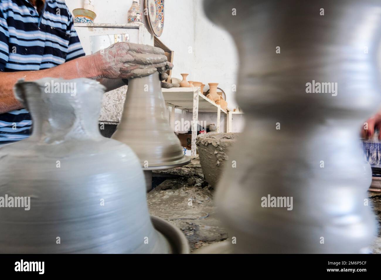 Skillful potter forming a vessel out of gray clay in a pottery factory ...