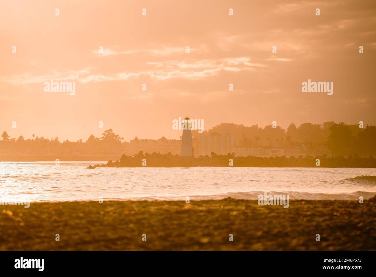 A lighthouse seen in the glowing sunset at a seashore Stock Photo - Alamy