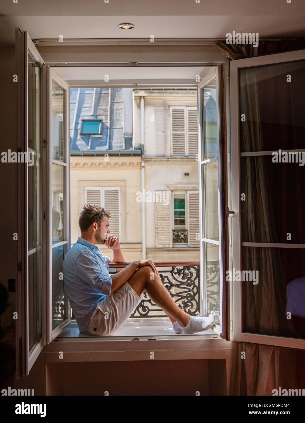 Young man sitting in a window looking out over the city Paris. Men ...