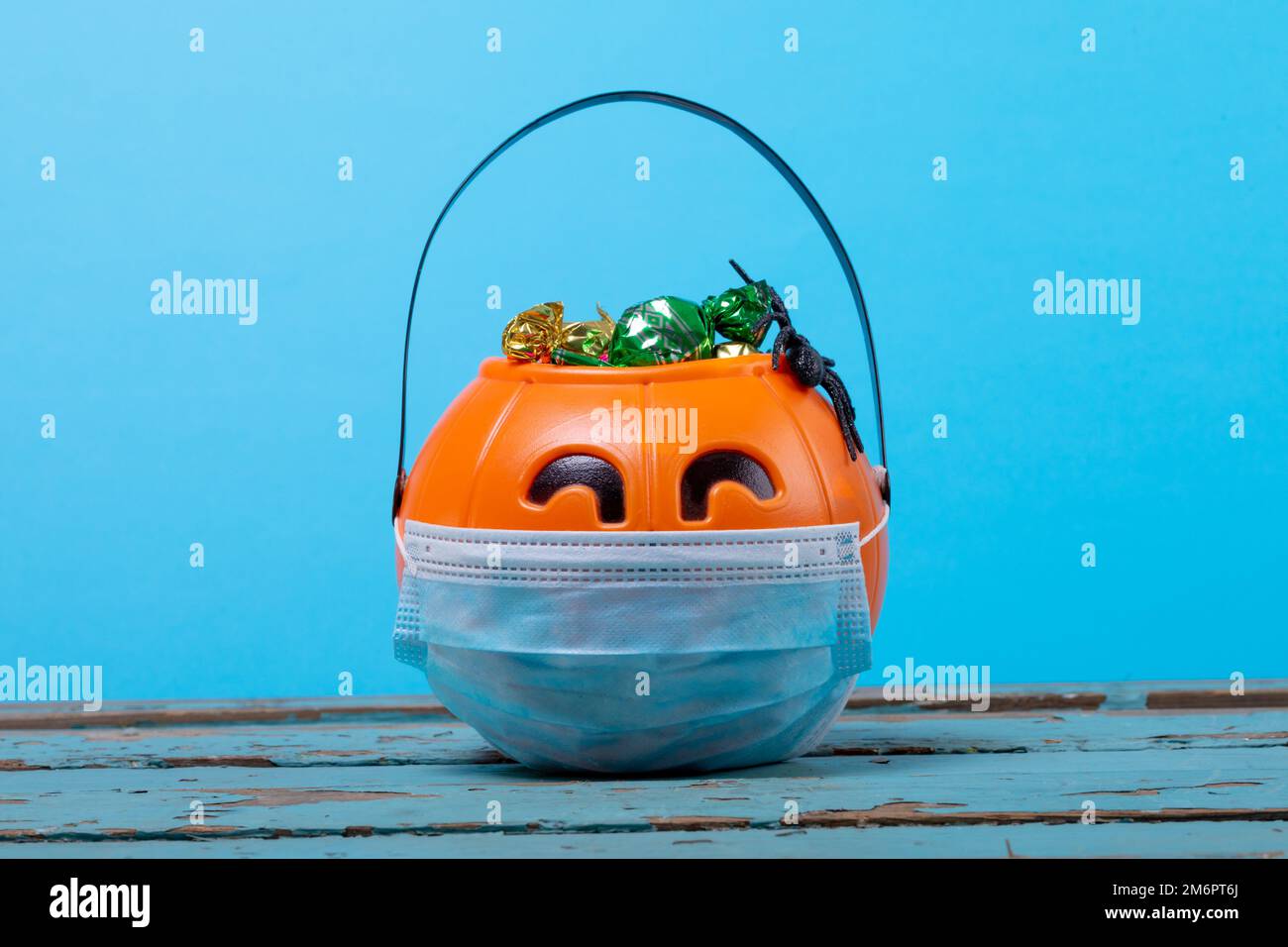 Face mask over pumpkin shaped bucket full of candies on wooden surface ...