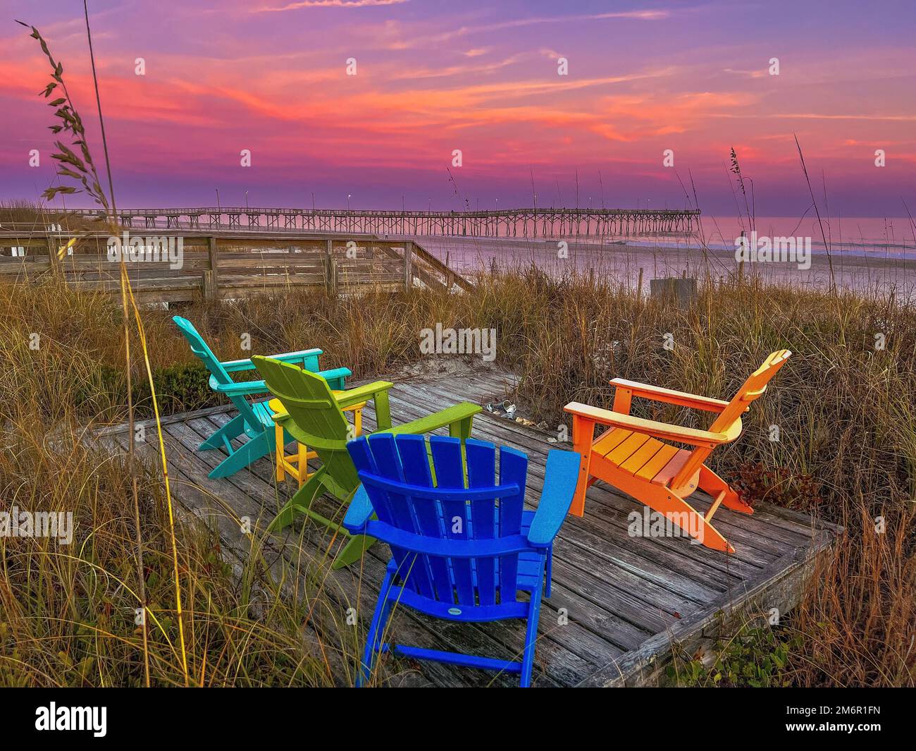 A wooden dock and colorful chairs at a beach during the sunset Stock ...