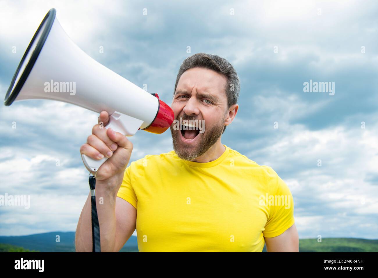 man in yellow shirt shout loud in loudspeaker on sky background Stock ...