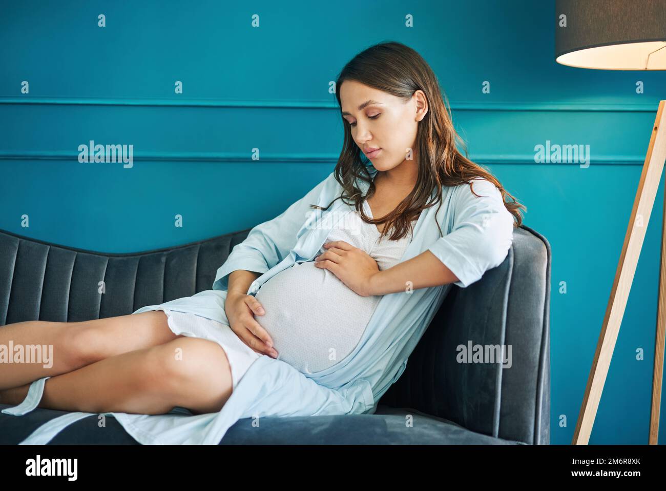Portrait of young pregnant woman touching her belly relax on sofa at ...