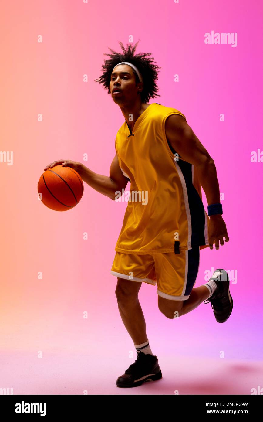 Image of biracial basketball player bouncing basketball on pink to ...