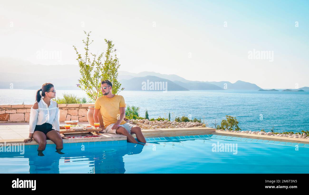 Couple men and women having breakfast by the pool looking out over ...