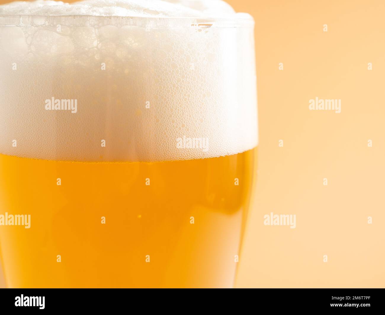Glass of beer with foam. Mug of beer on an orange background. Close-up ...