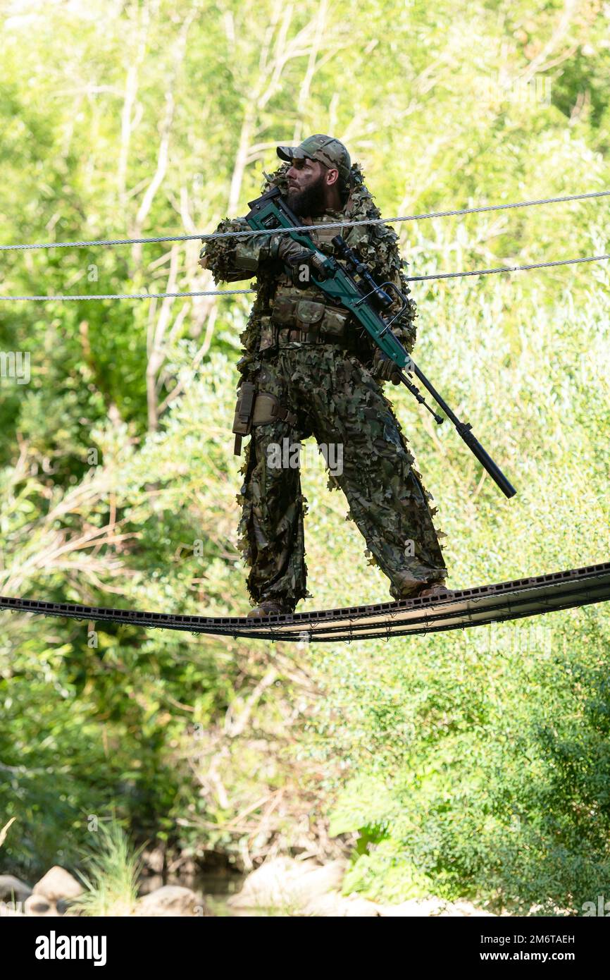 A military man or airsoft player in a camouflage suit sneaking the rope ...
