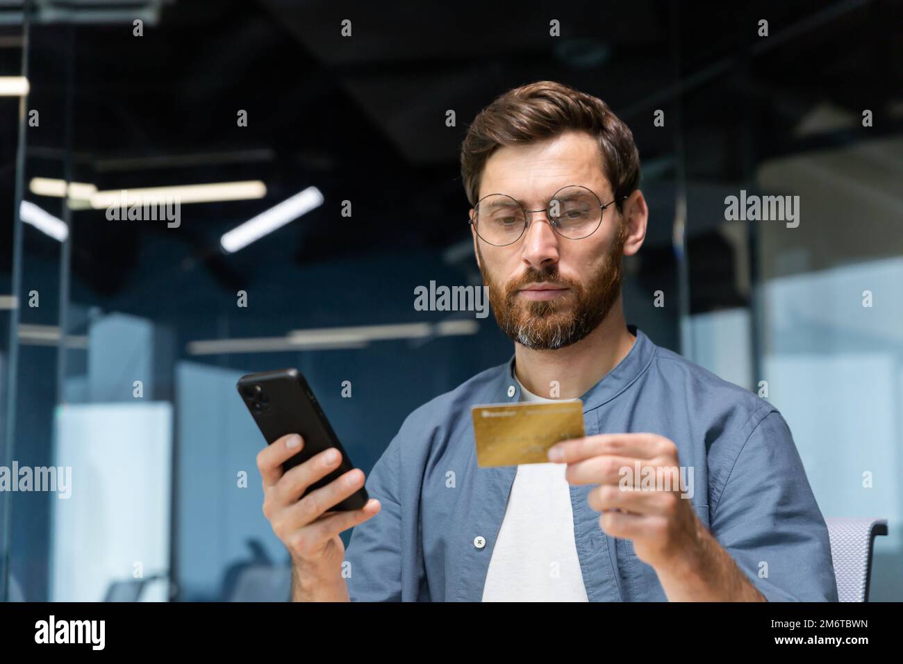 Serious thinking man inside office holding bank credit card and ...