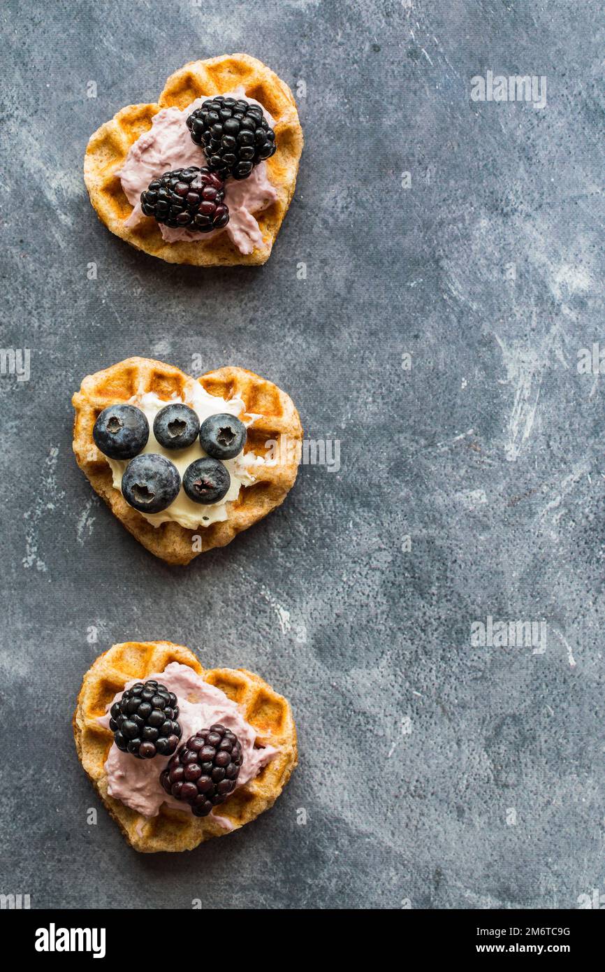 Three mini heart shaped waffles with cream cheese spread and berries on ...