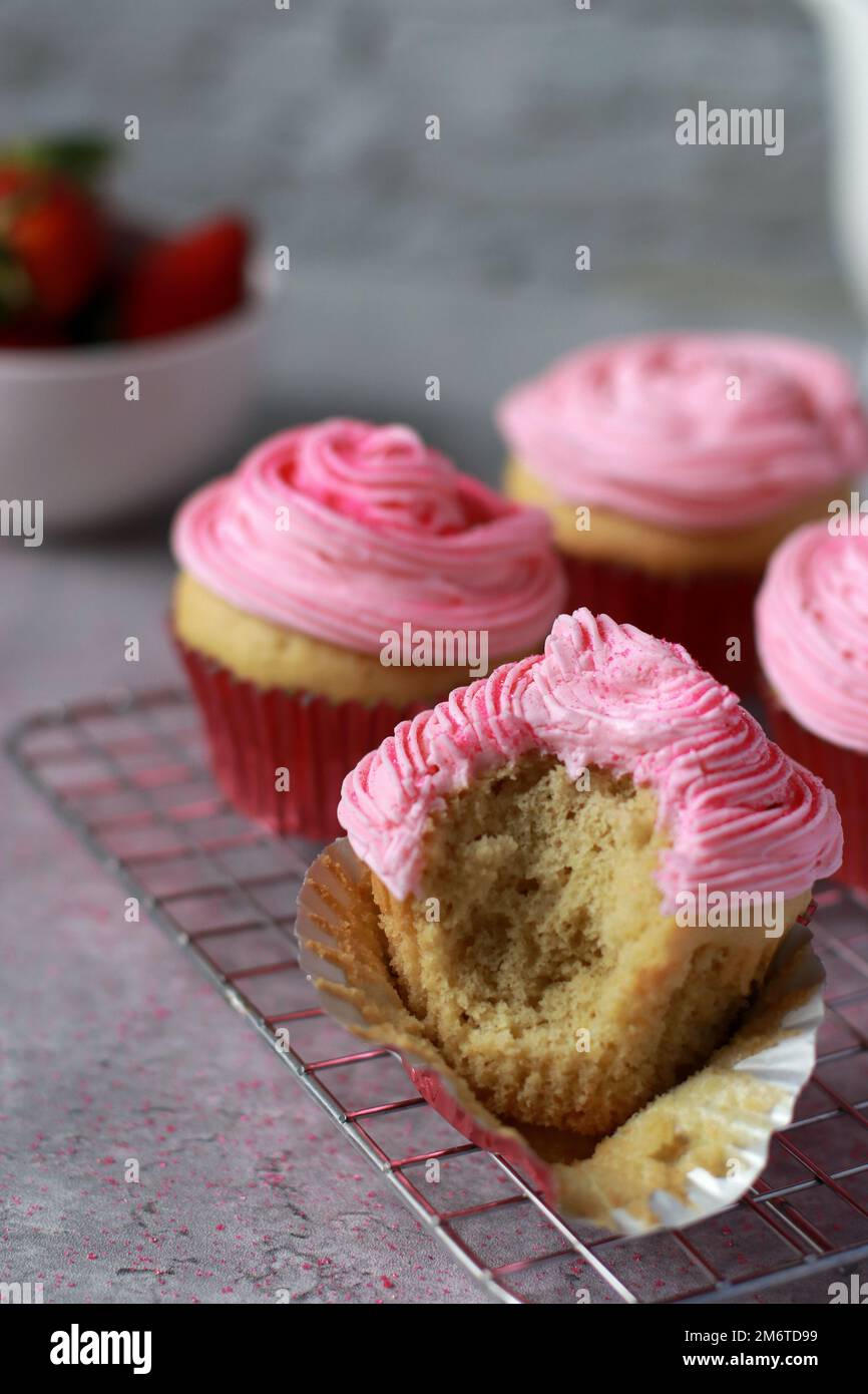 Close up of bitten muffin with pink sprinkles and buttercream frosting ...