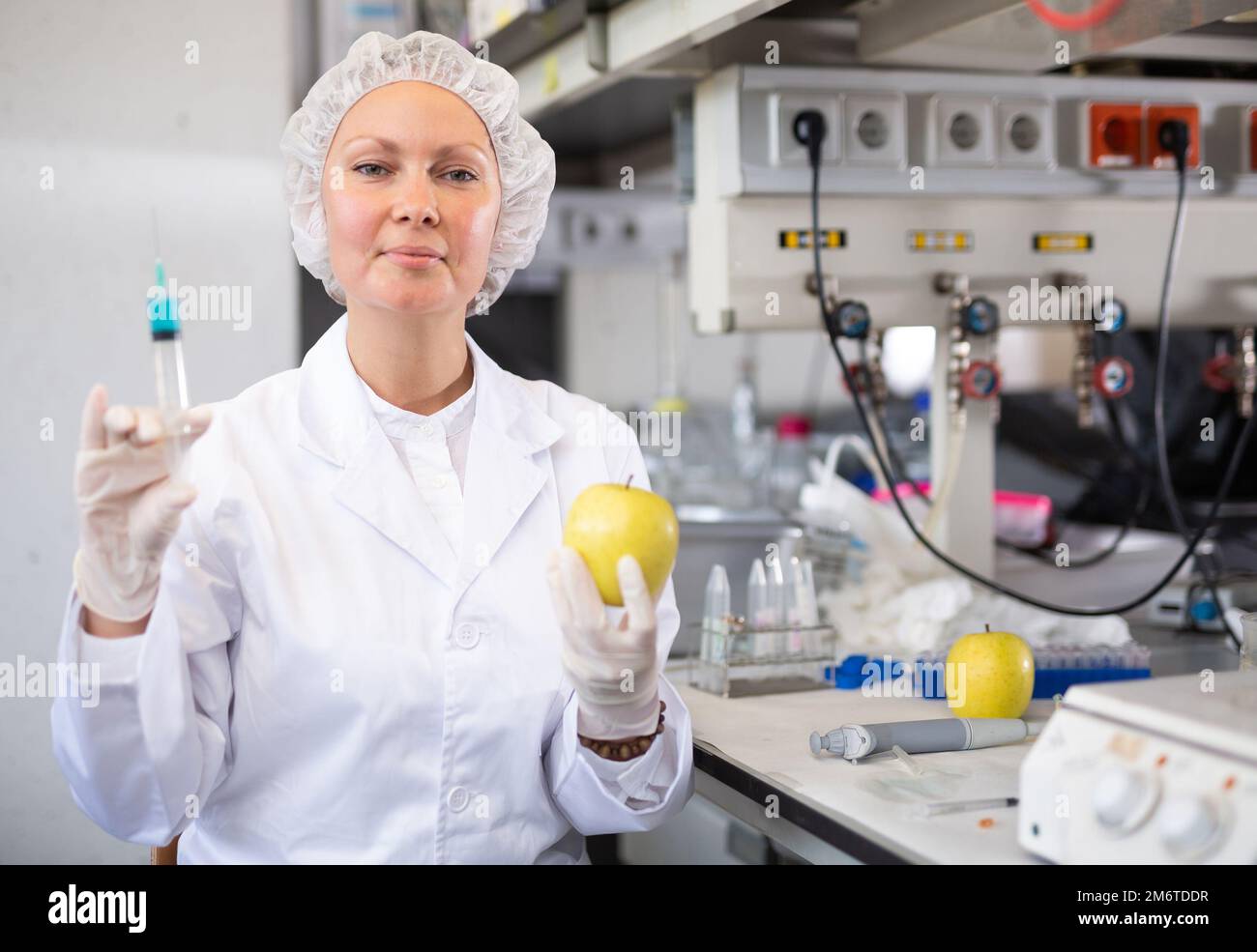 Middle-aged female scientist holding syringe and apple in research ...