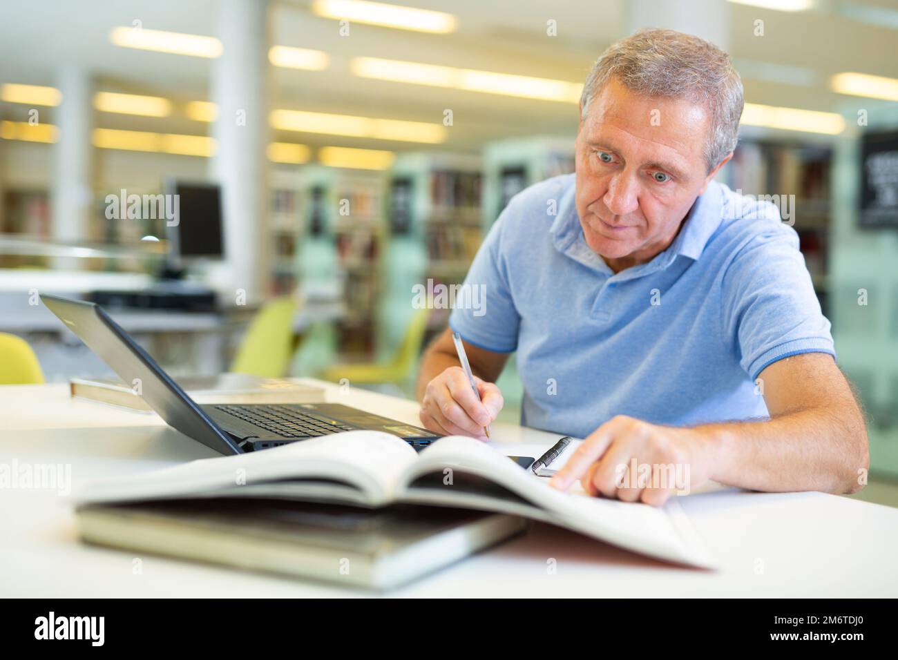 Focused casual mature male writing in notepad and reading books in the ...