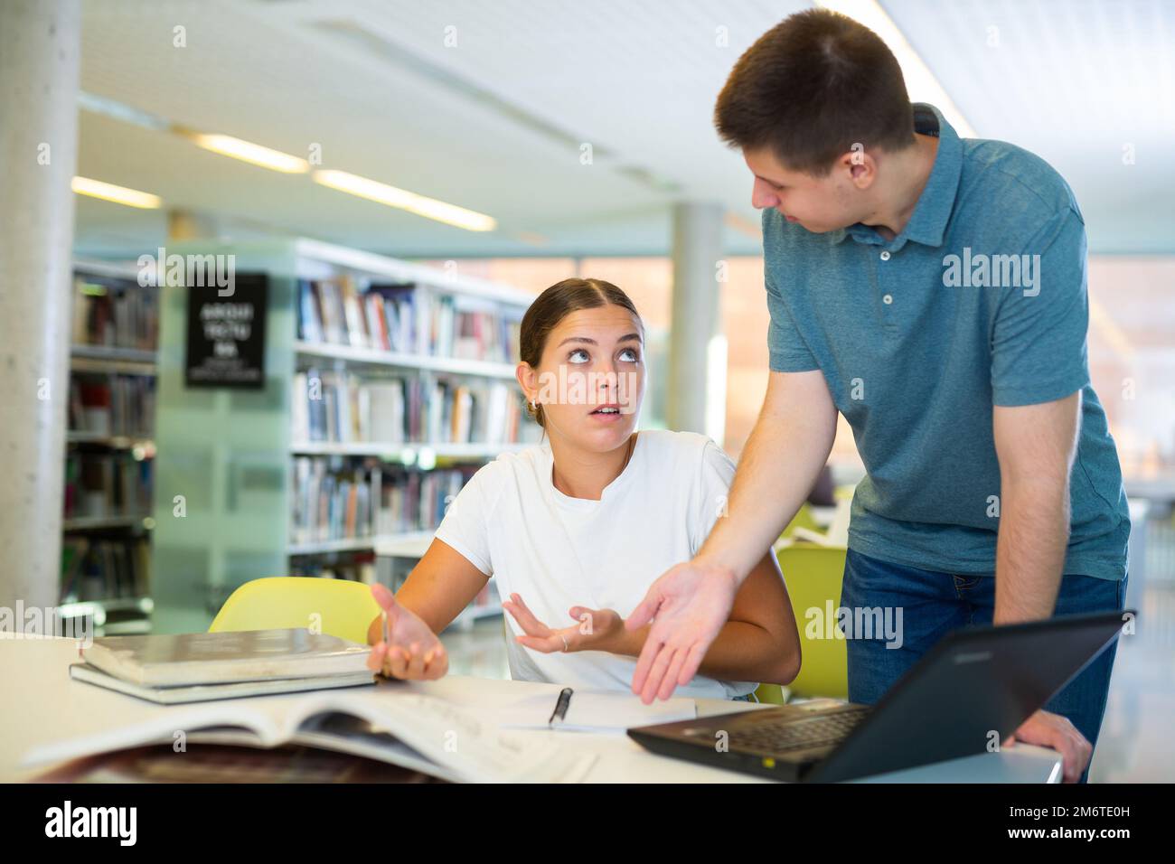 Friendly young woman offering assistance to male friend studying ...