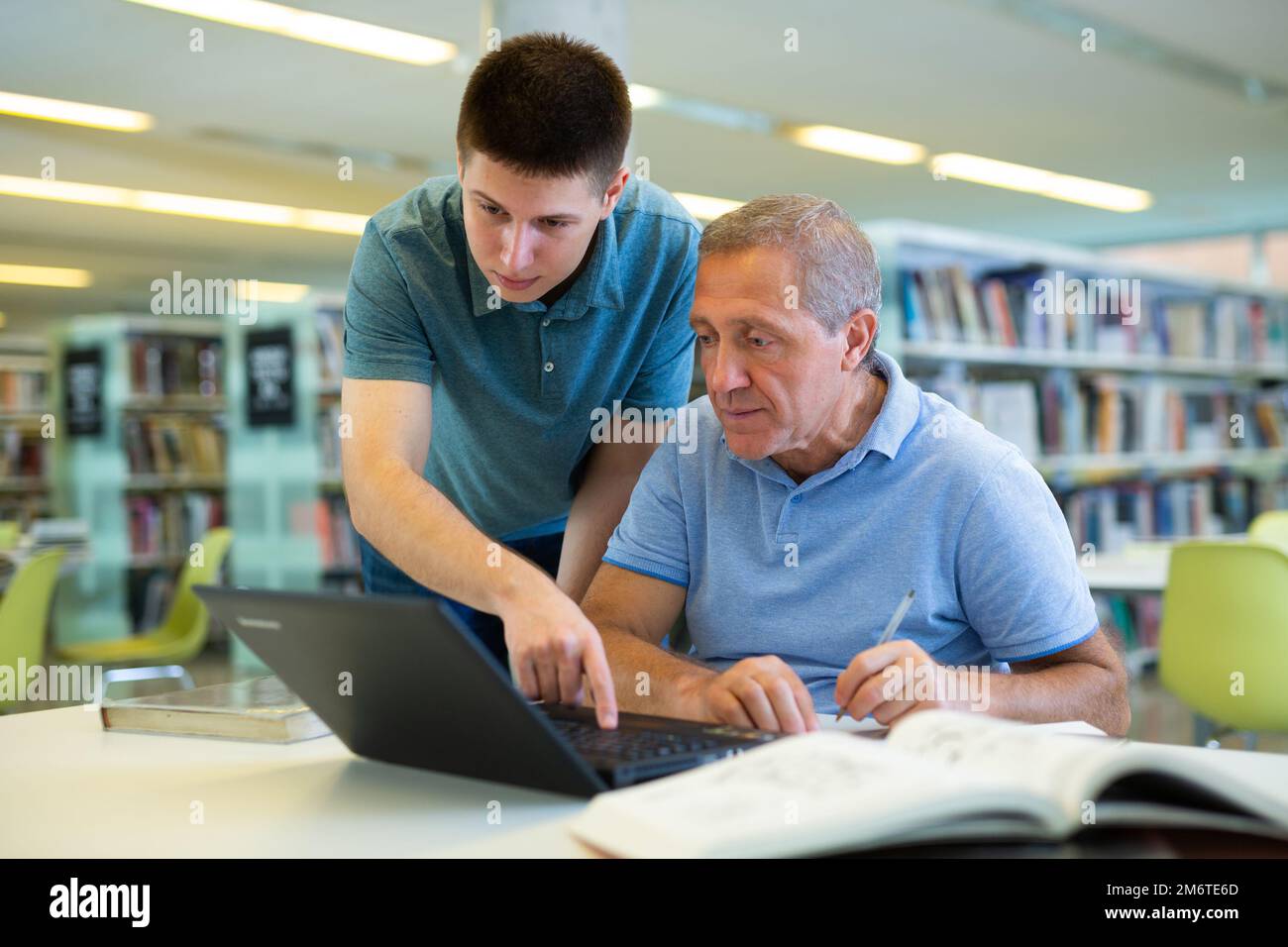 Young guy helping older man in laptop interface in library Stock Photo ...