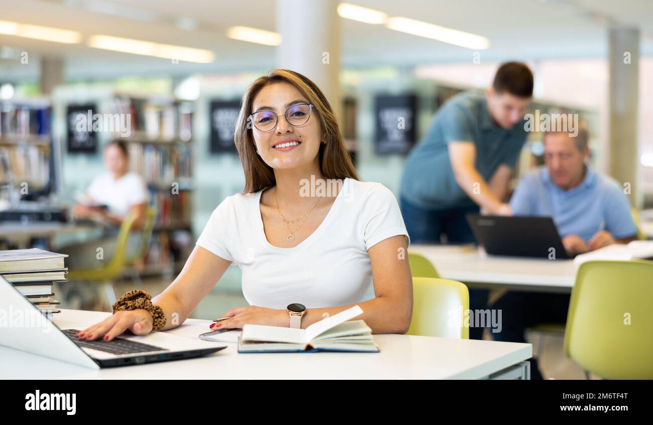 Confident student girl studying in the university library on a laptop ...
