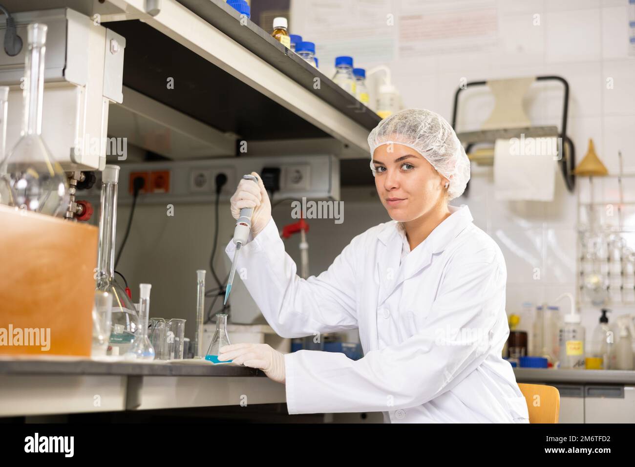 Clever female researcher in white coat mixing reagents in test tube ...