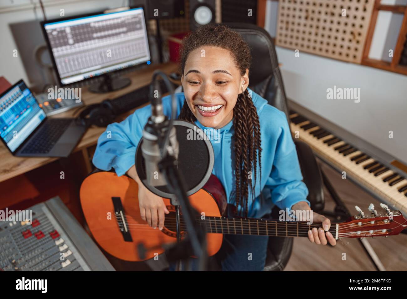 Stylish African pretty woman playing guitar and singing into microphone ...