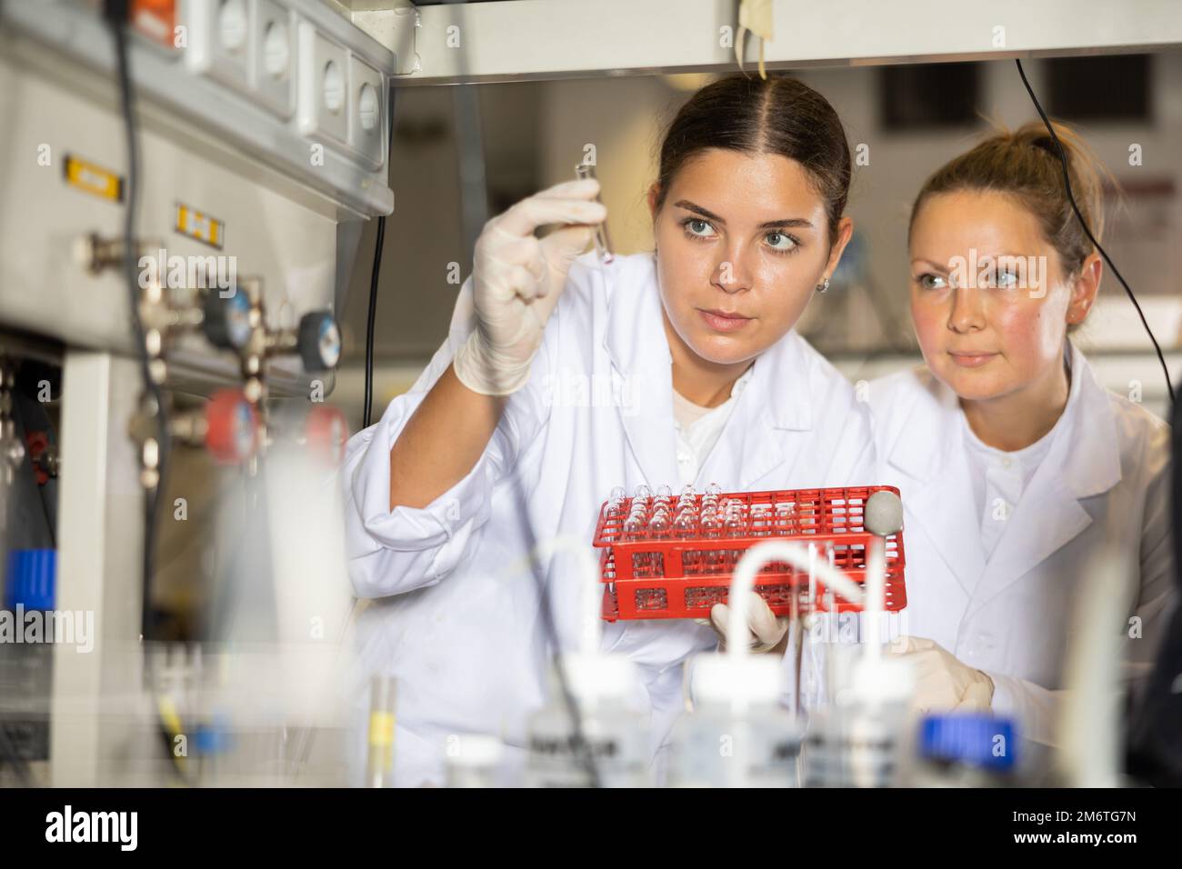 Female biochemists holding tripod and examining solution in test tube ...
