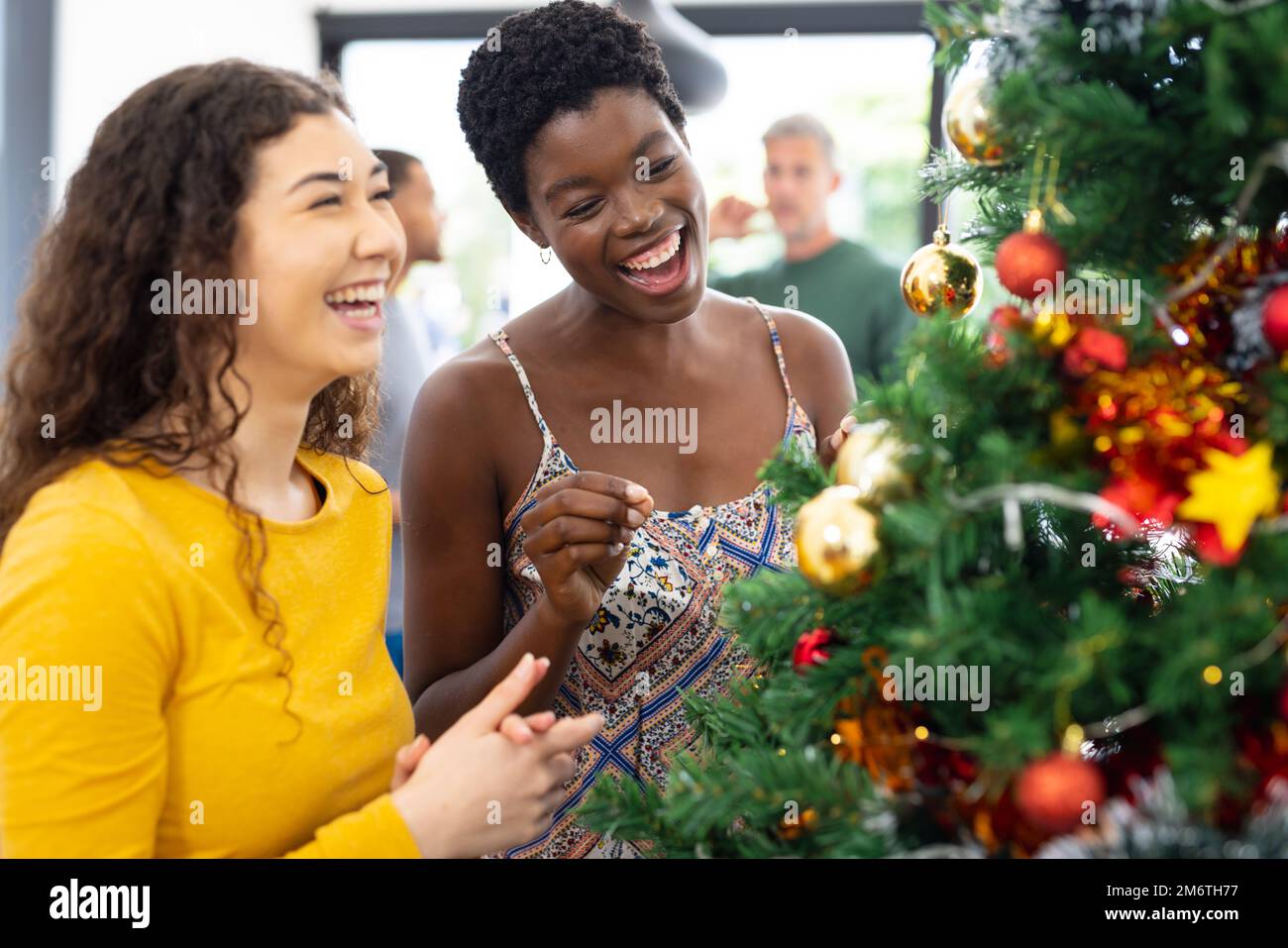 Happy diverse female friends decorating christmas tree at christmas ...