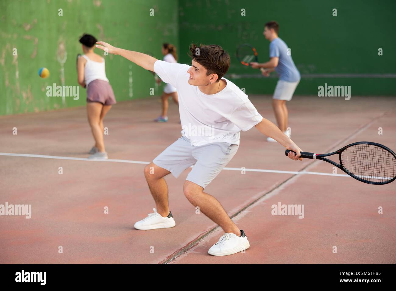 Young hispanic frontenis player swinging racquet to hit ball on outdoor ...