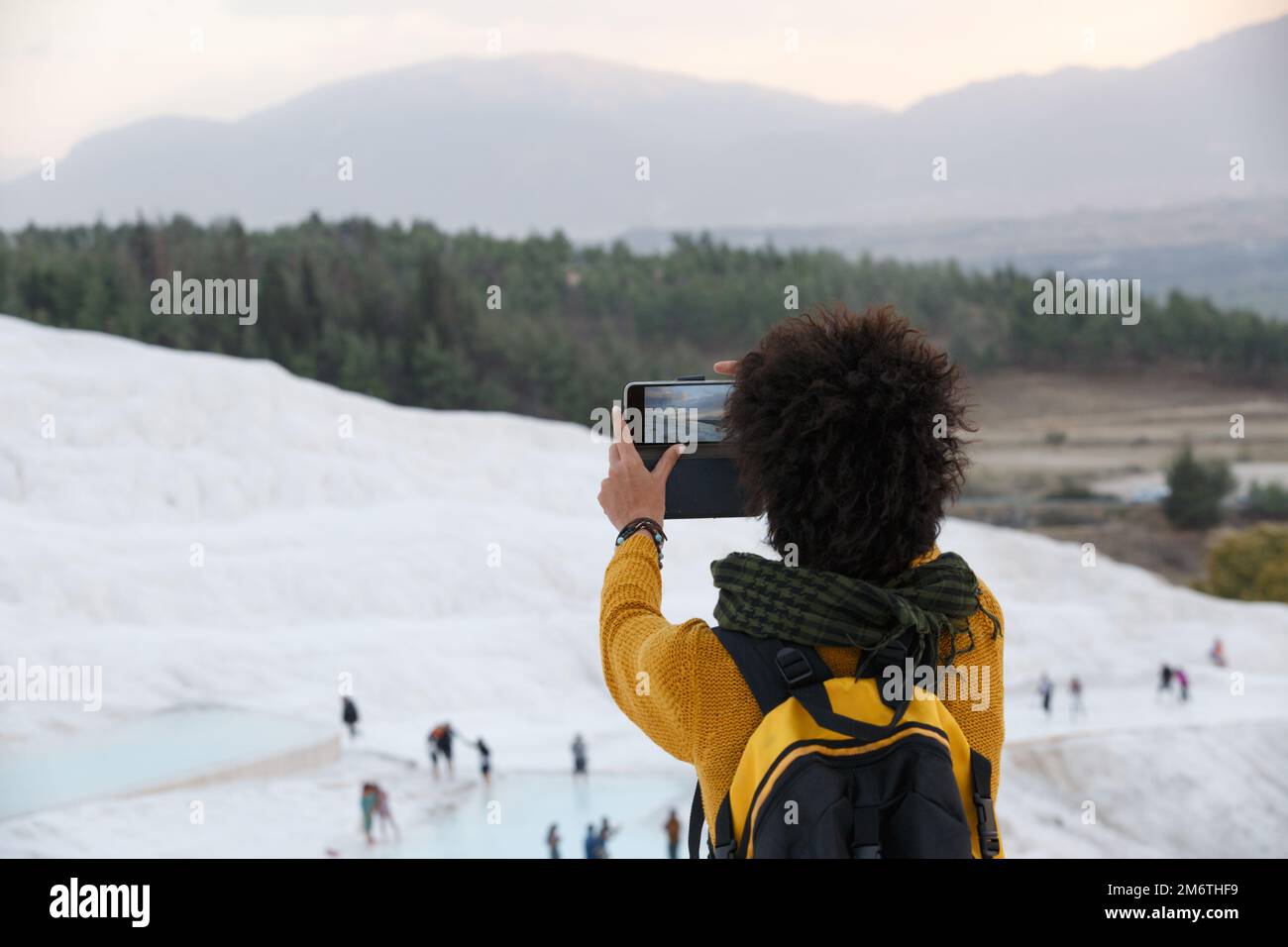 A girl with curly hair takes a smartphone photo of the scenery of ...