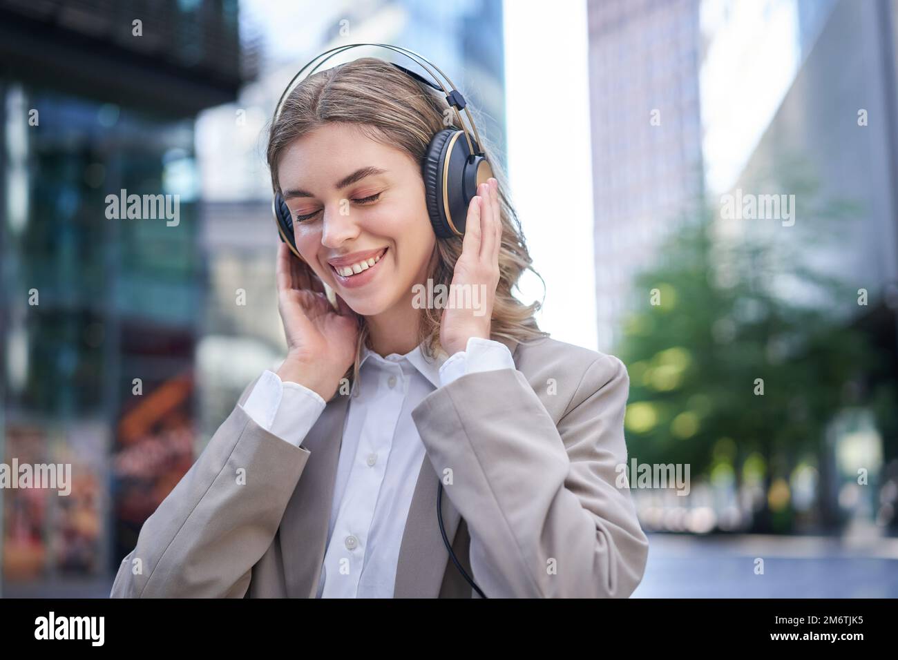 Portrait of smiling corporate woman, girl in suit listening music in ...