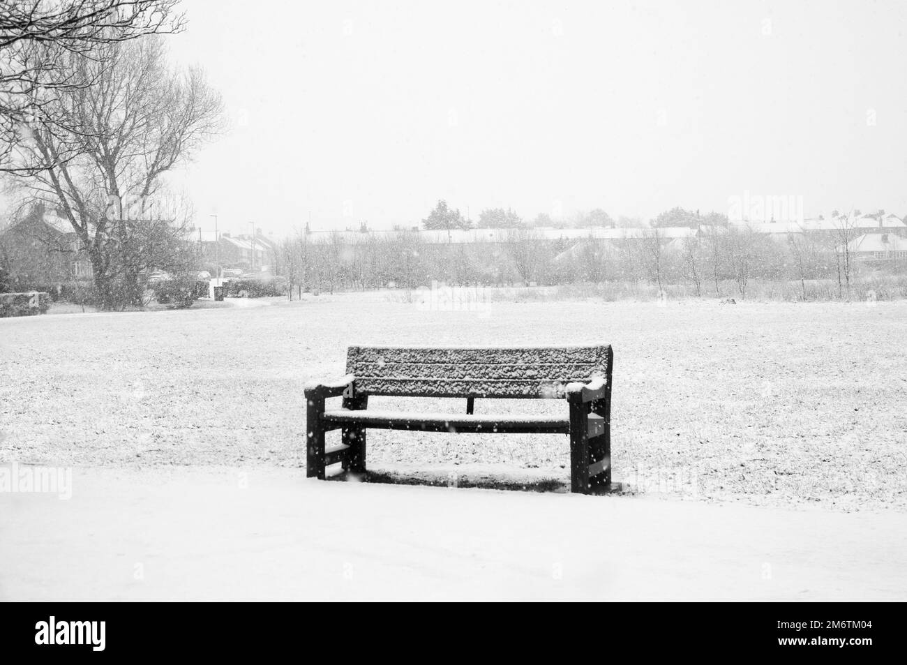 Snow scene of lone wooden park bench with snow falling on ground and ...