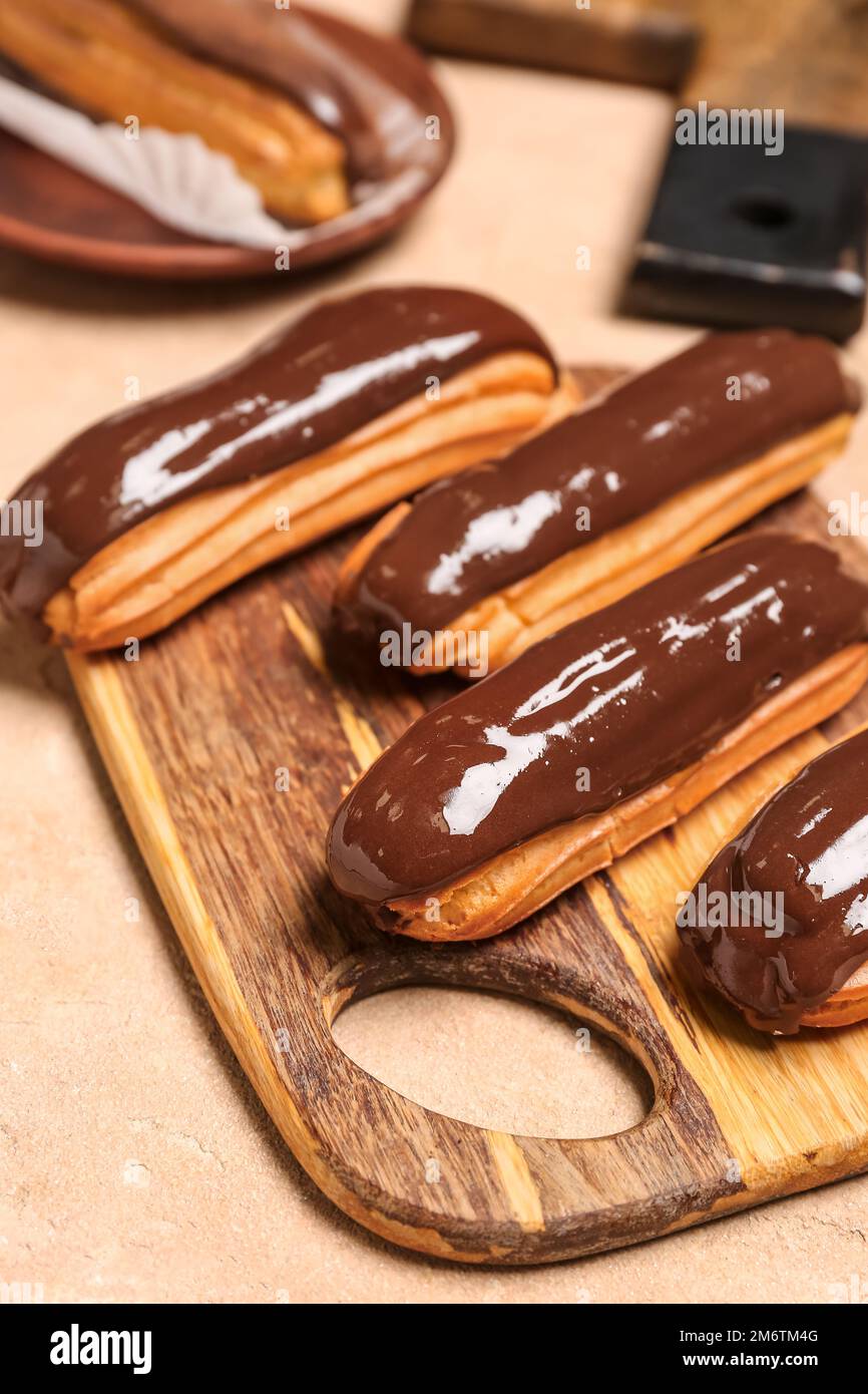 Wooden board with tasty chocolate eclairs on color background, closeup ...