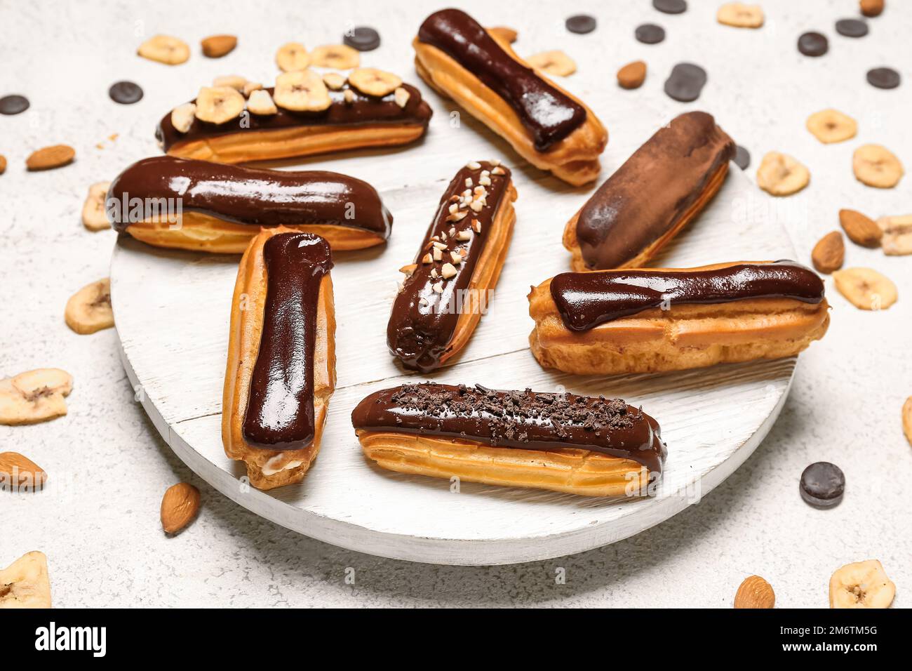Wooden board with tasty chocolate eclairs, almond nuts and banana chips ...