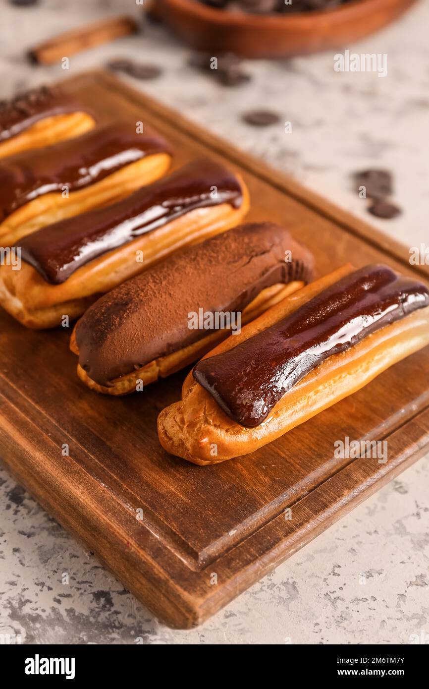 Wooden board with tasty chocolate eclairs on light background, closeup ...