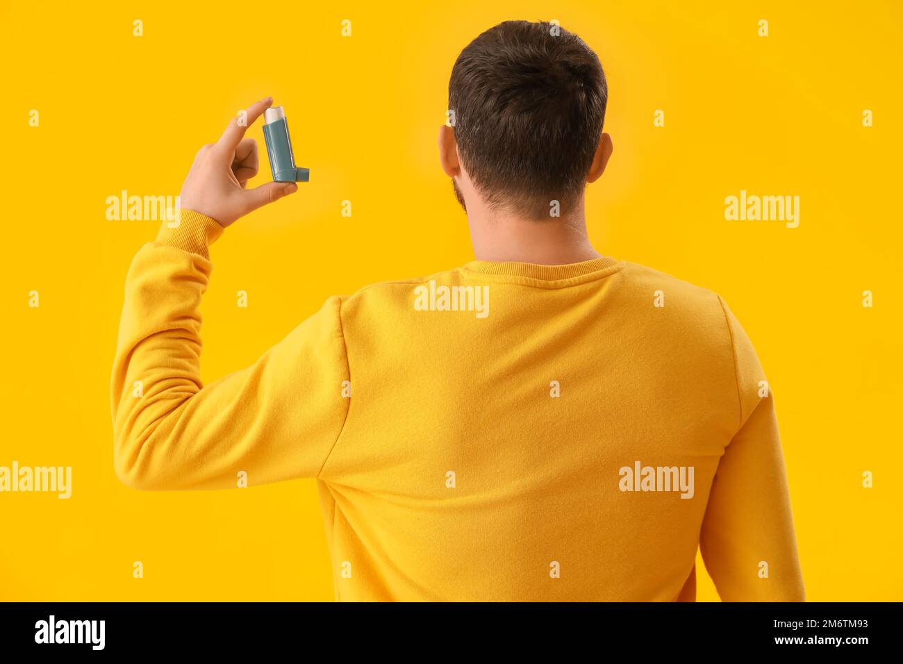 Man with inhaler on yellow background, back view Stock Photo - Alamy