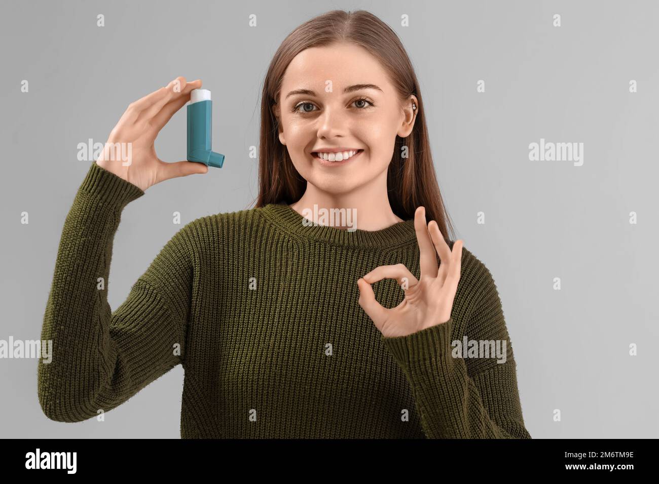 Young woman with inhaler showing OK on grey background Stock Photo - Alamy