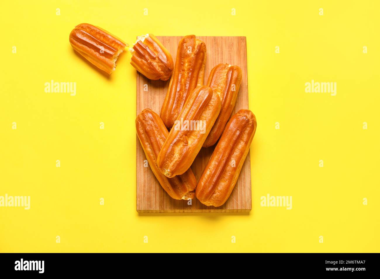 Wooden board with sweet eclairs on yellow background Stock Photo - Alamy