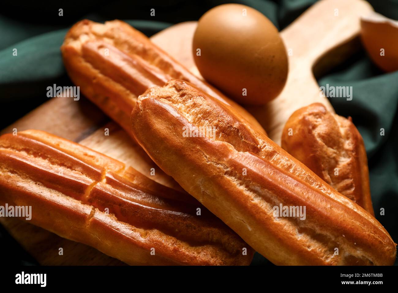 Wooden board with tasty eclairs and egg on dark fabric background ...