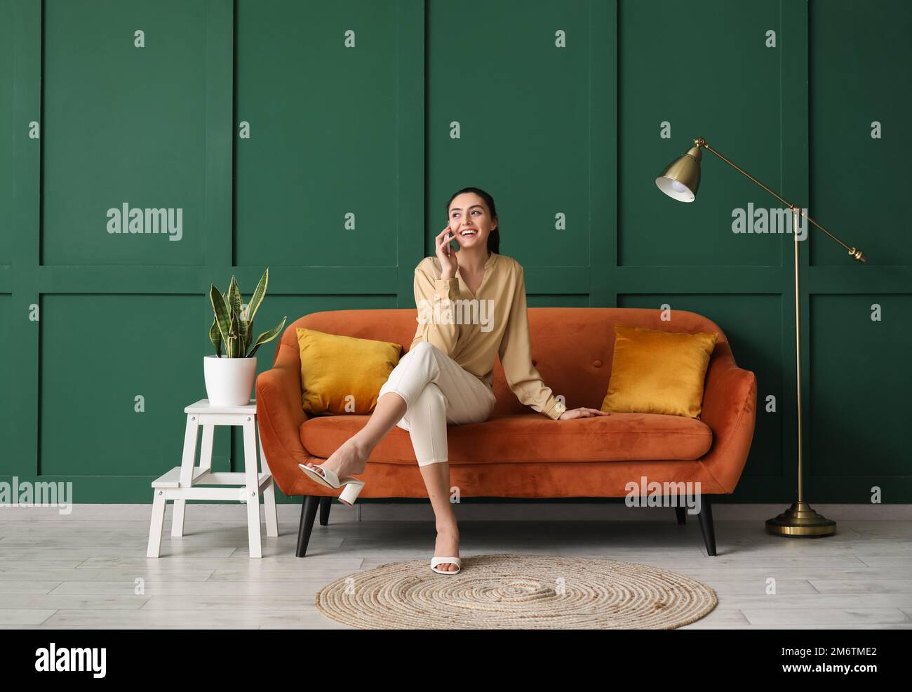 Young woman talking by mobile phone on red sofa near green wall Stock ...