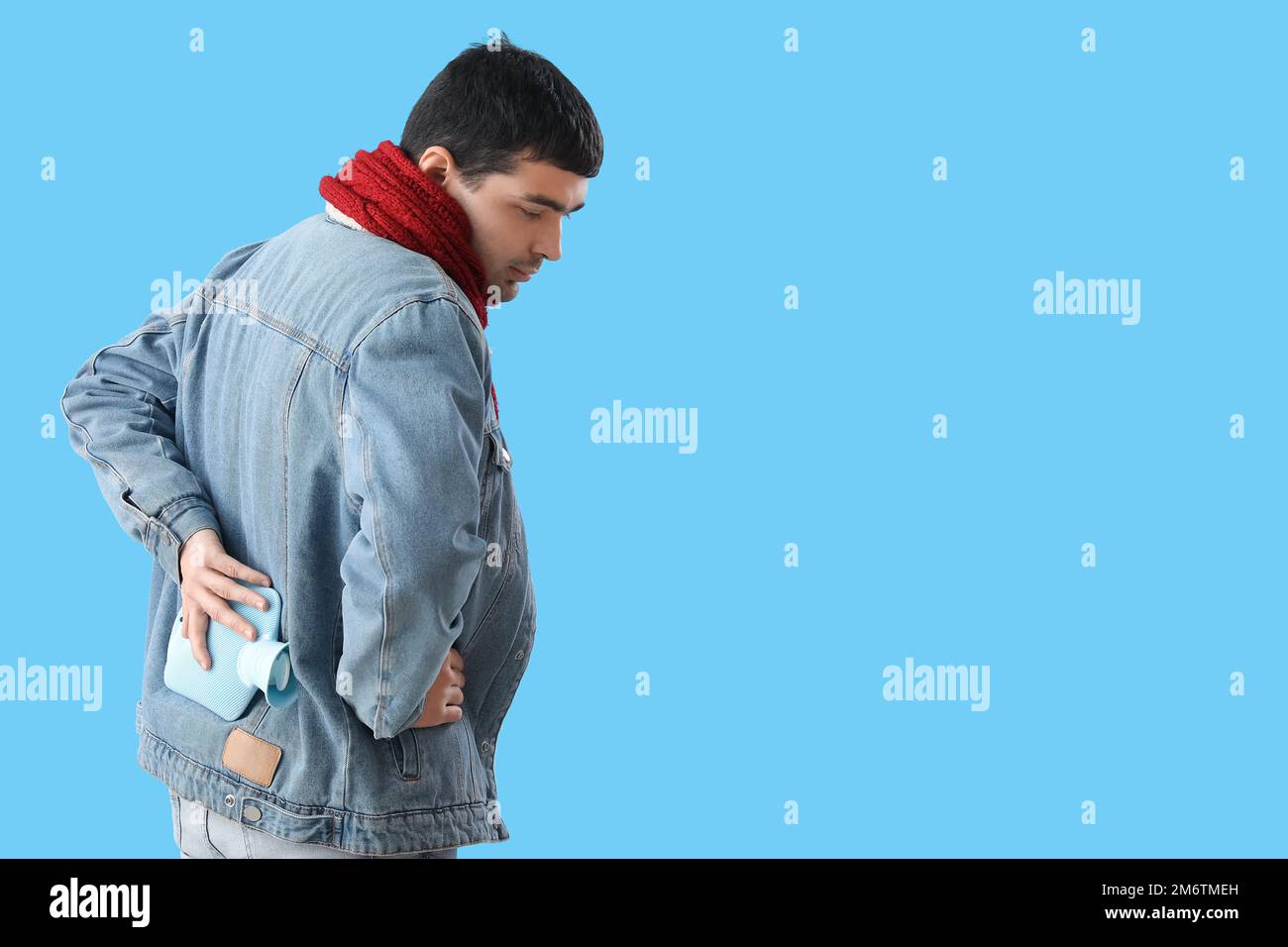 Young man warming his lower back with hot water bottle on blue ...