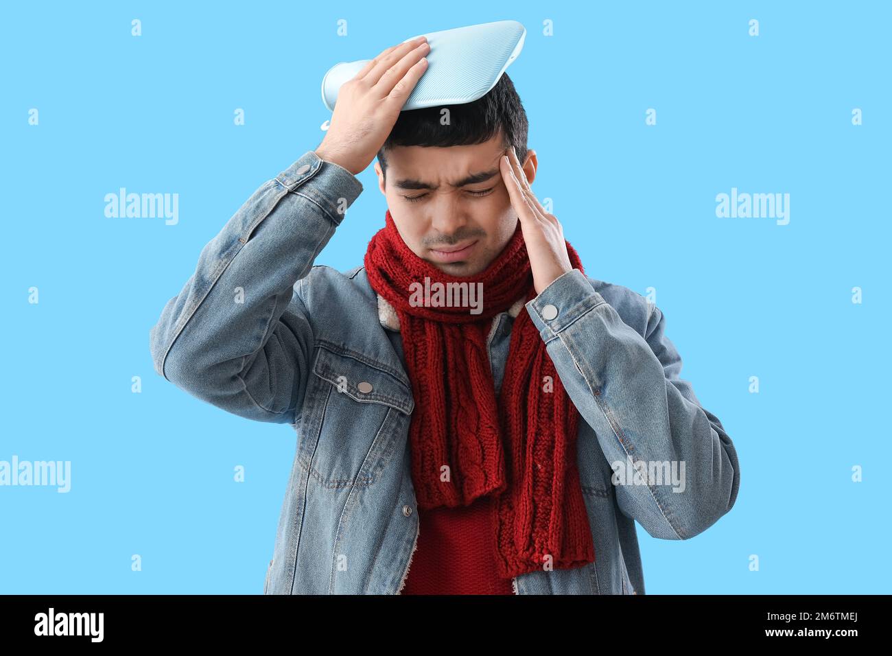 Young man warming his head with hot water bottle on blue background ...