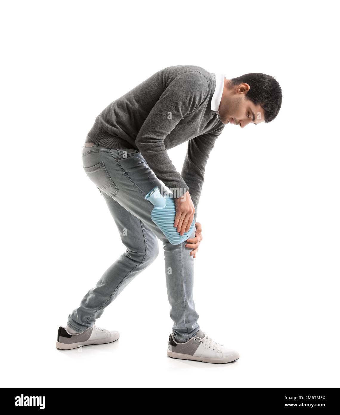 Young man warming his knee with hot water bottle on white background ...