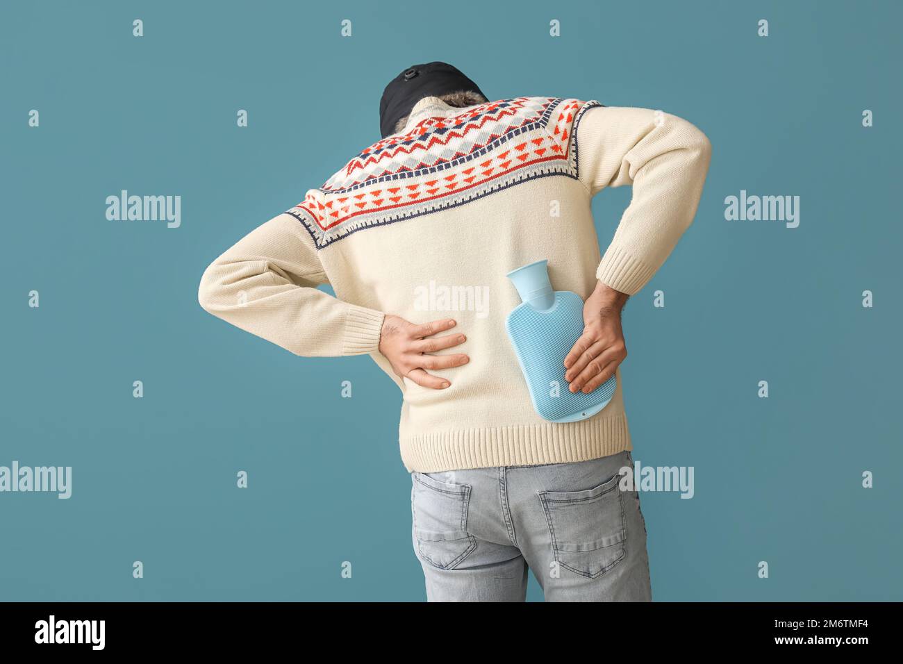 Young man warming his lower back with hot water bottle on color ...