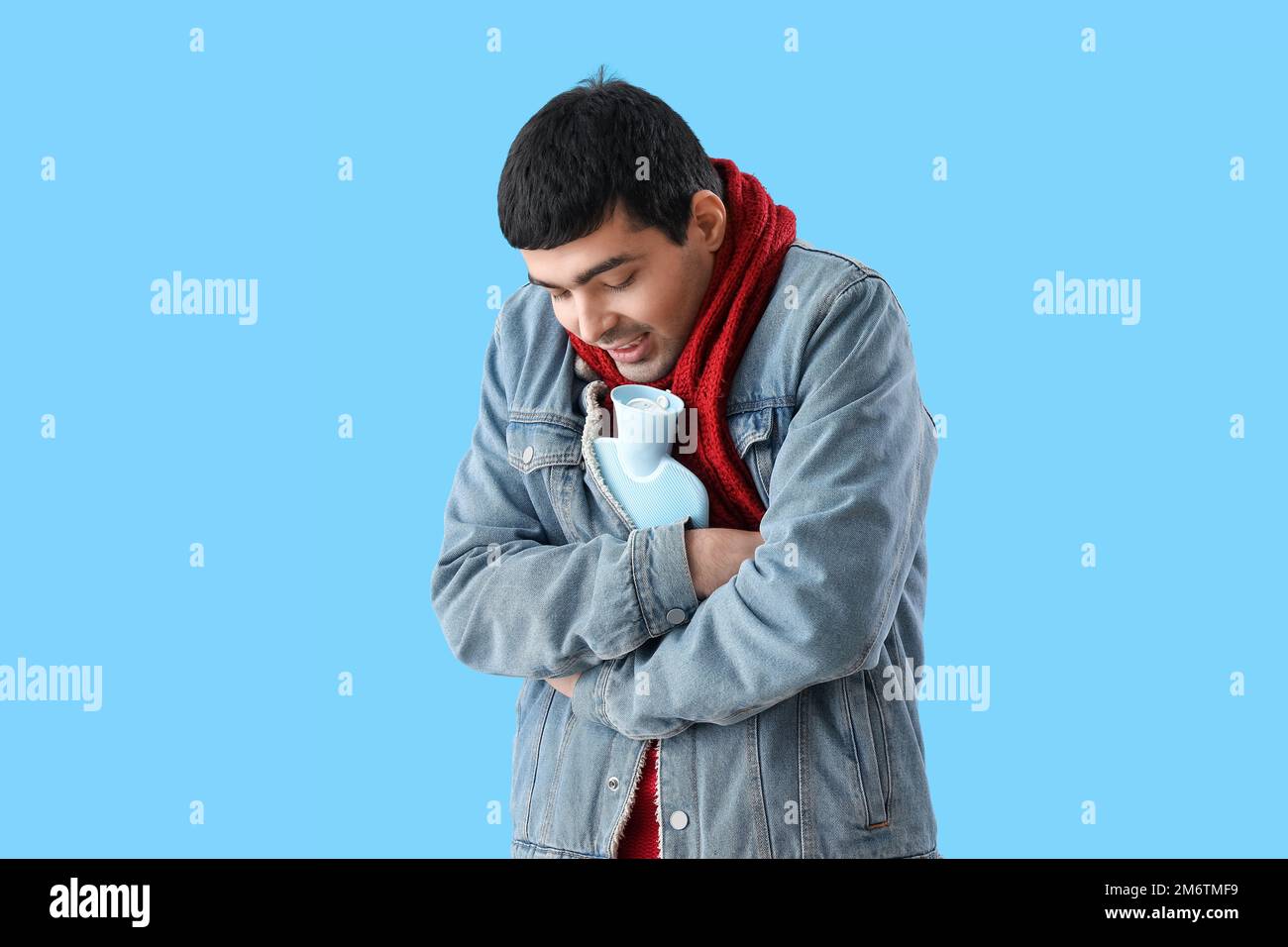 Young man warming with hot water bottle on blue background Stock Photo ...