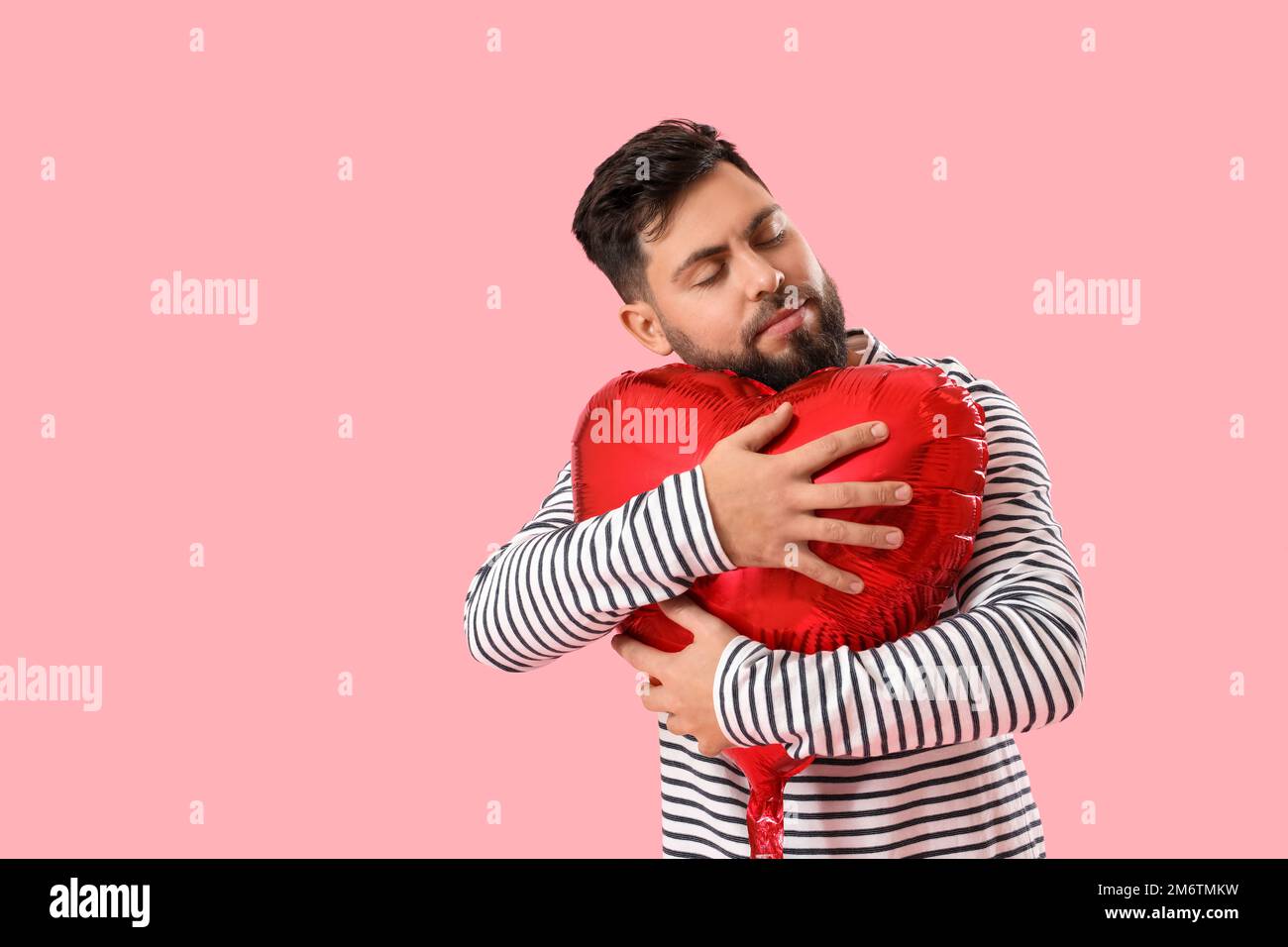 Young bearded man hugging balloon for Valentine's Day on pink ...