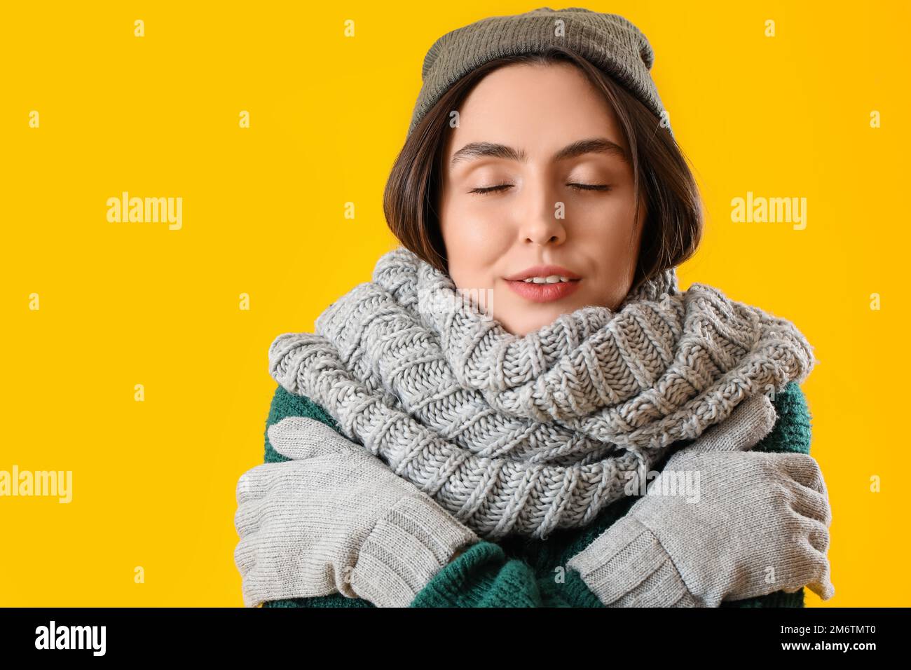 Frozen young woman in winter clothes on yellow background, closeup ...