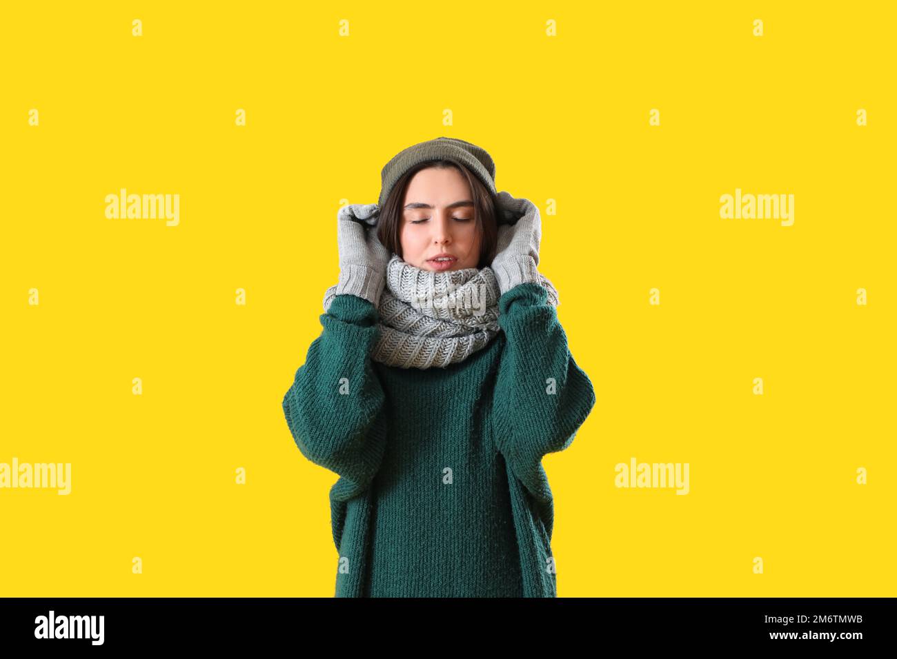 Frozen young woman in winter clothes on yellow background Stock Photo ...