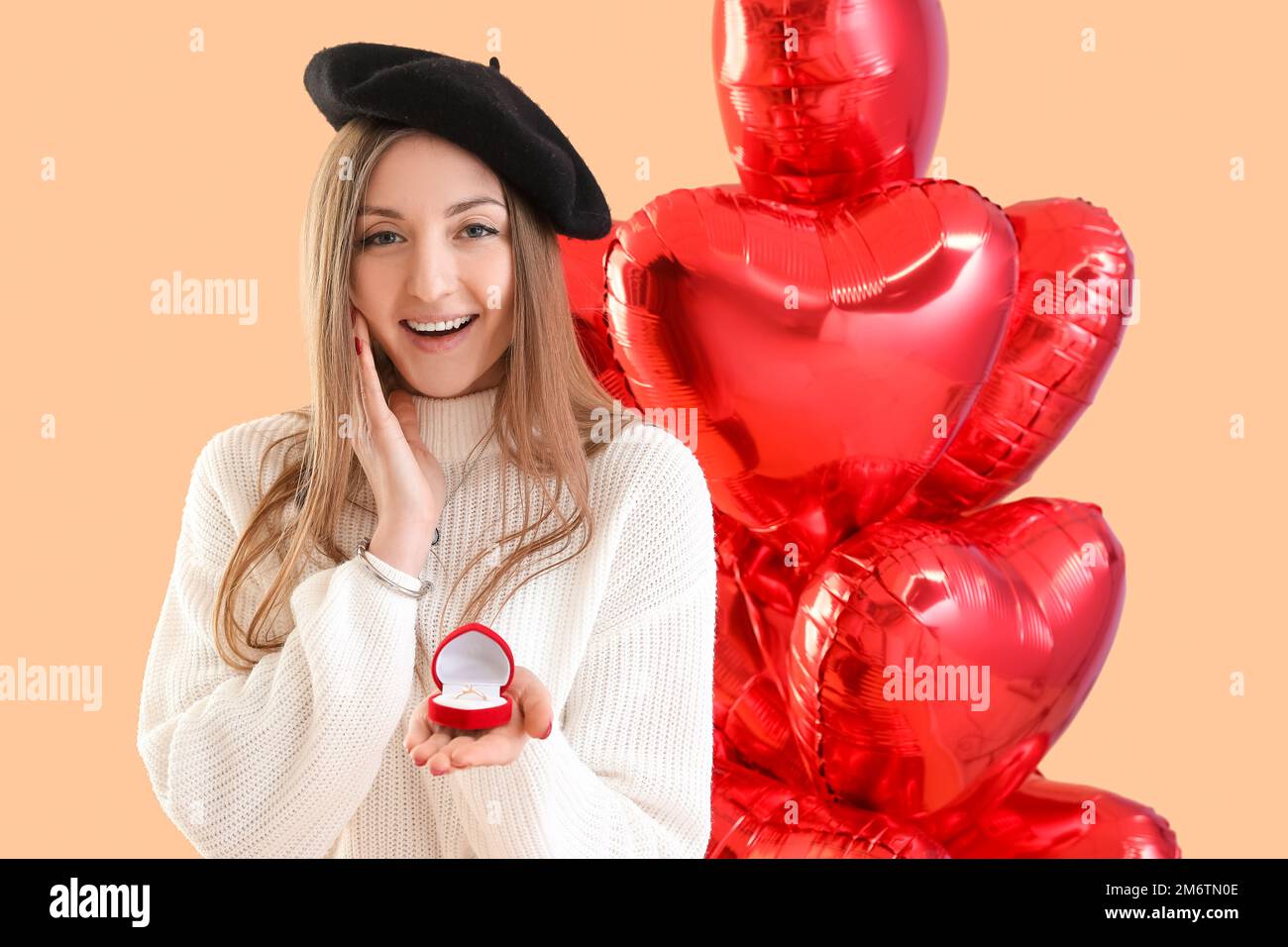 Happy young woman with engagement ring and balloons on beige background ...