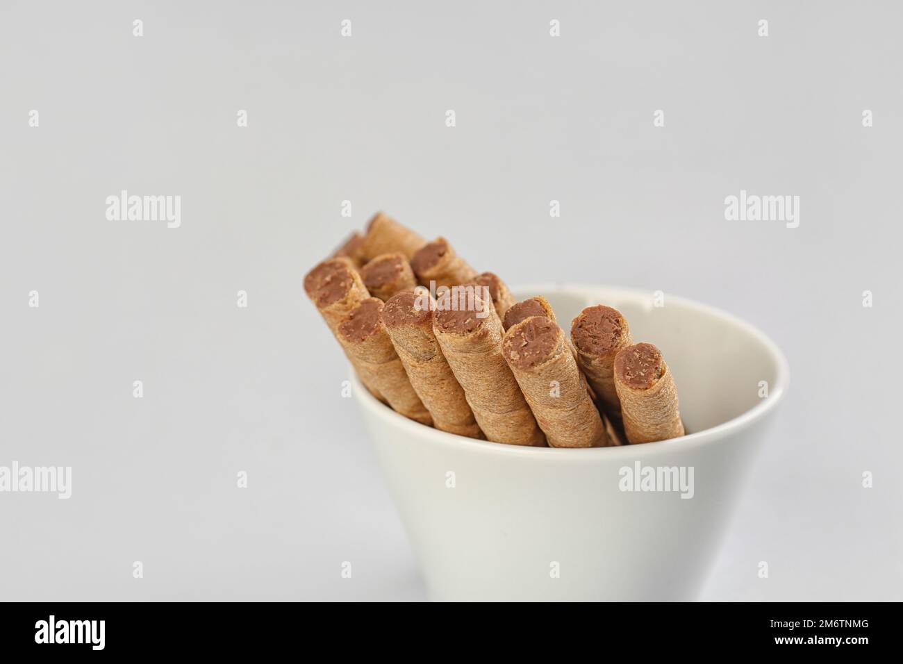 Bowl of tasty wafer rolls with condensed boiled milk on grey background ...