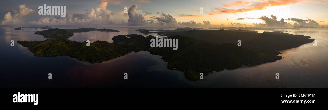Sunrise illuminates clouds that drift over the calm waters of the ...