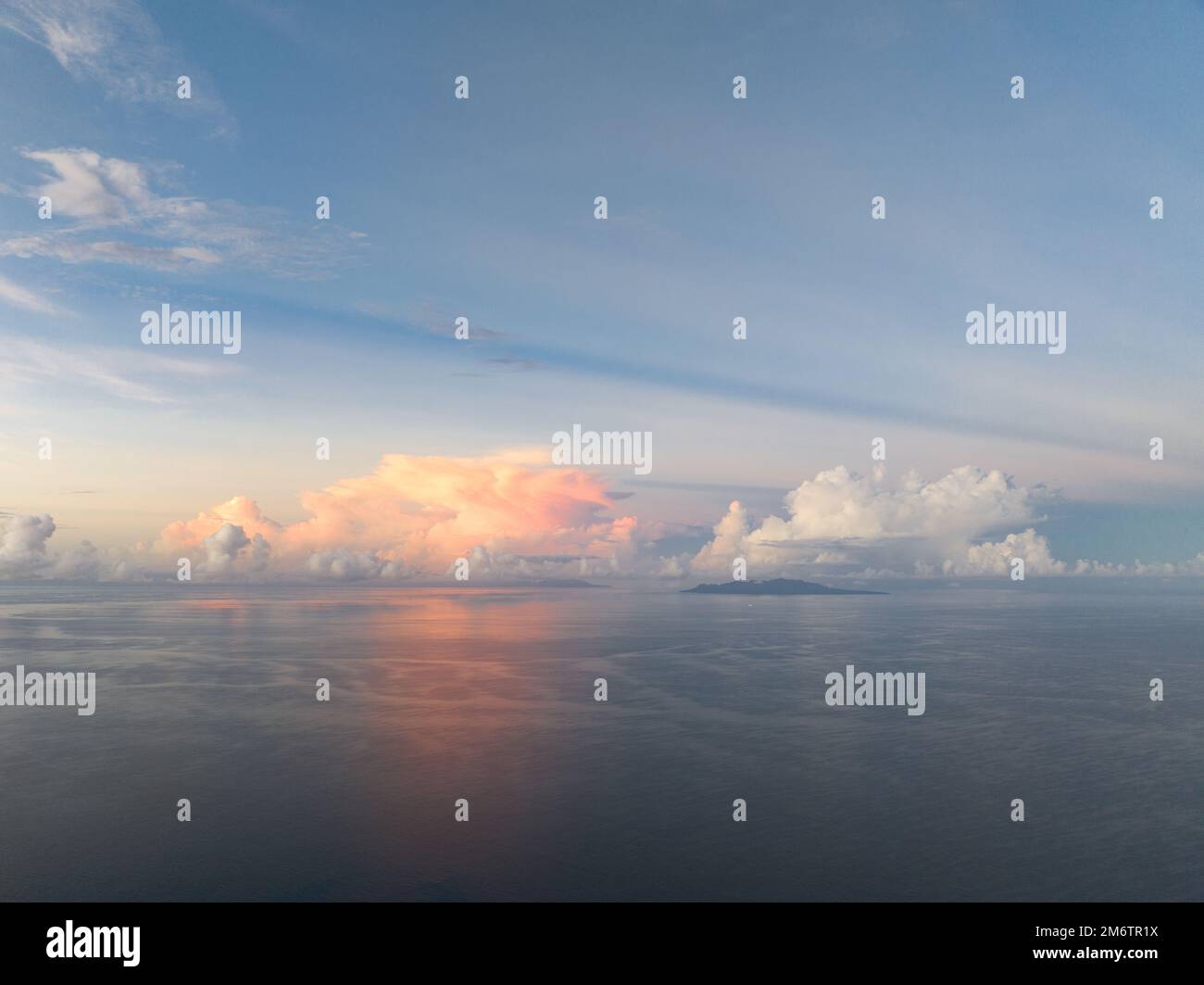 Sunrise illuminates clouds that drift over the calm waters of the ...
