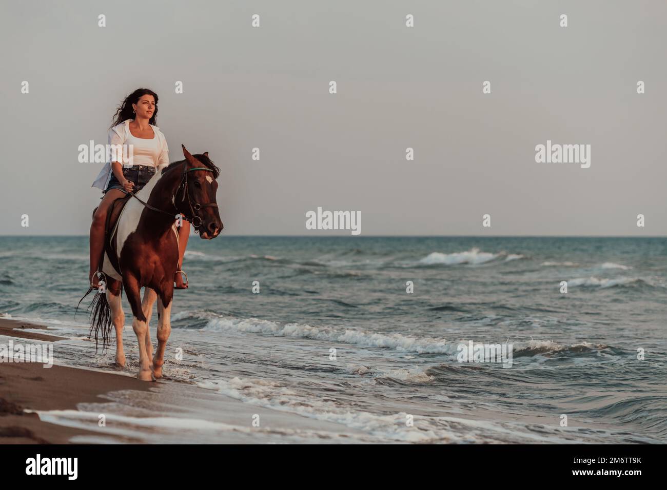 Woman in summer clothes enjoys riding a horse on a beautiful sandy ...