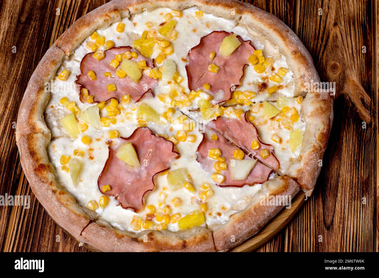 Delicious pizza with ham, pineapple, corn on a creamy base on woden ...