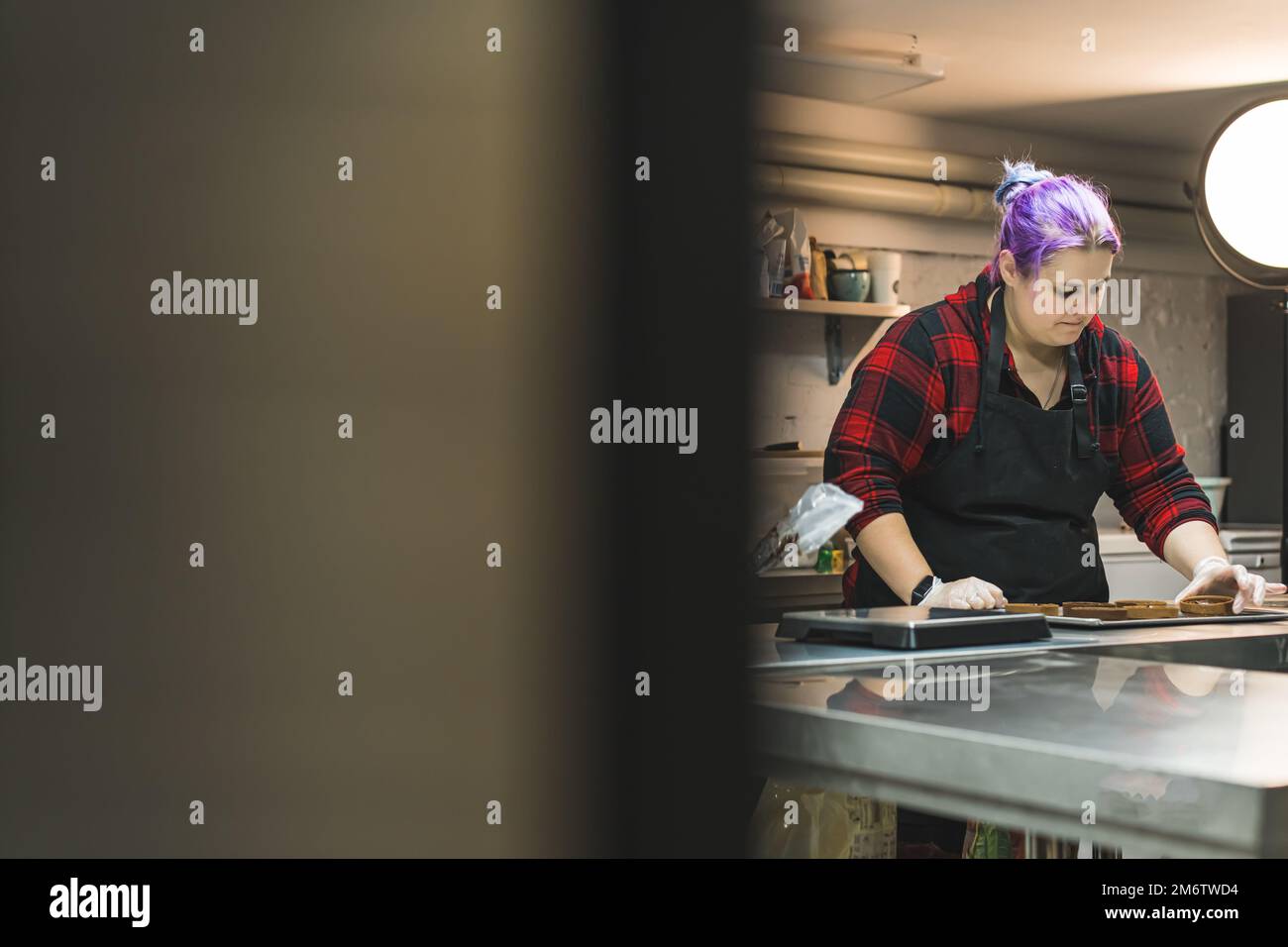 Female baker wearing red plaid shirt and black apron is preparing ...